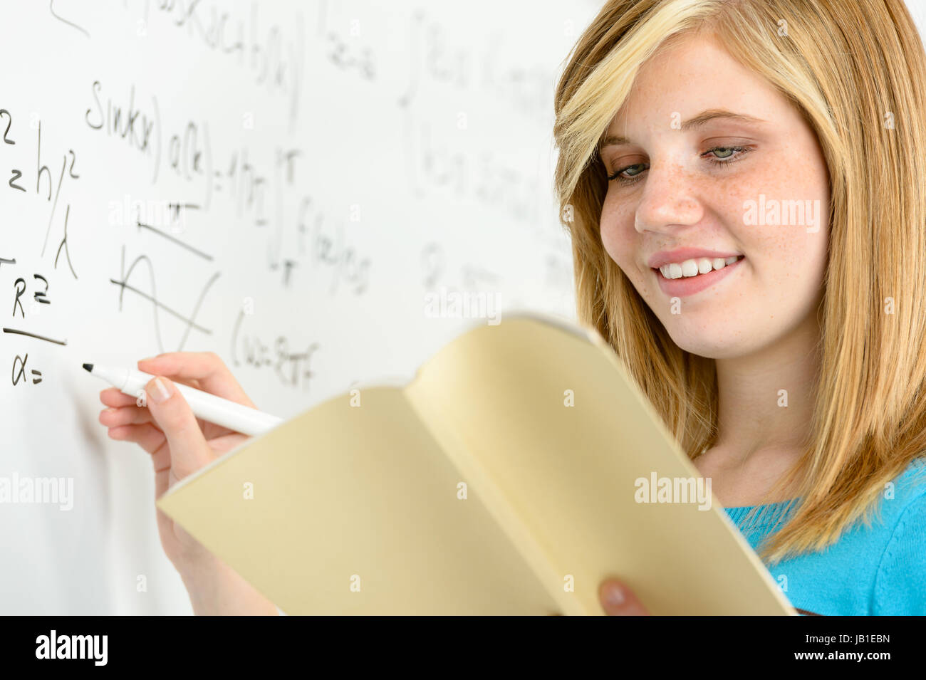 Student girl writing maths on white board looking in book Stock Photo ...