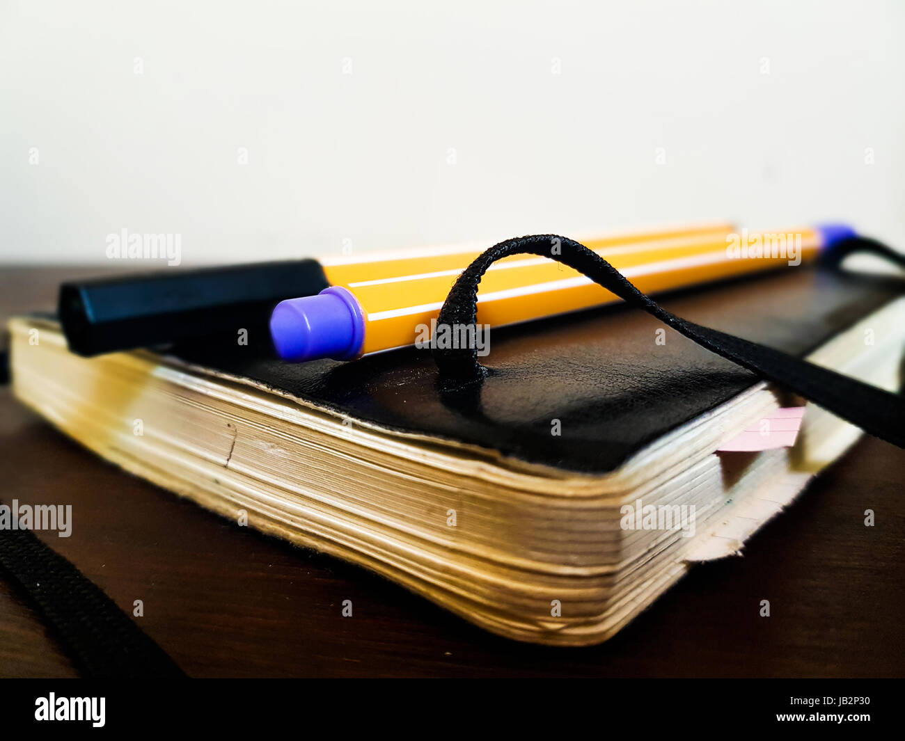 A closed notebook on a desk with two pens on top Stock Photo - Alamy