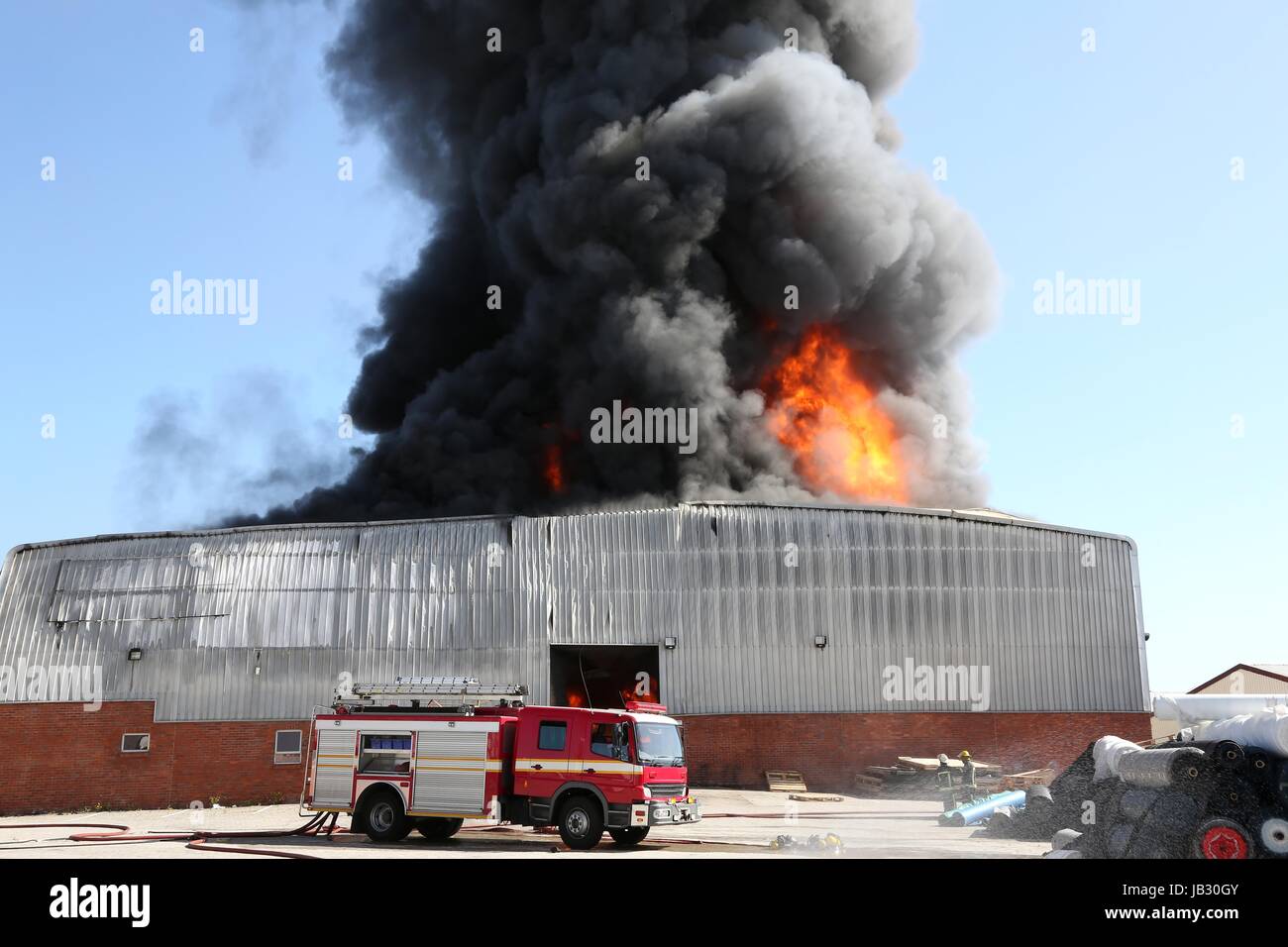 Warehouse building burning with intense flames and firemen attending ...