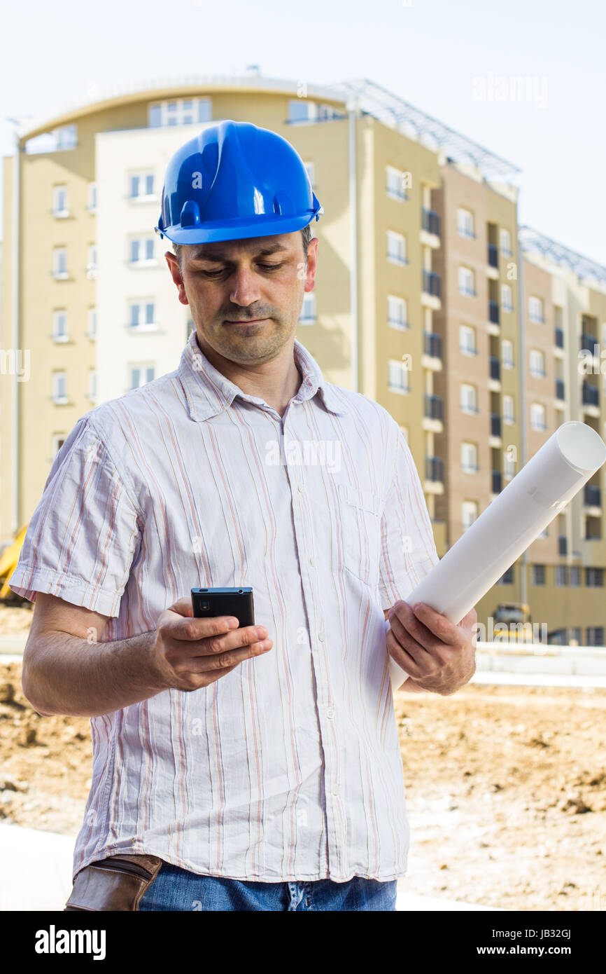 Construction manager holding project and using phone on building site ...