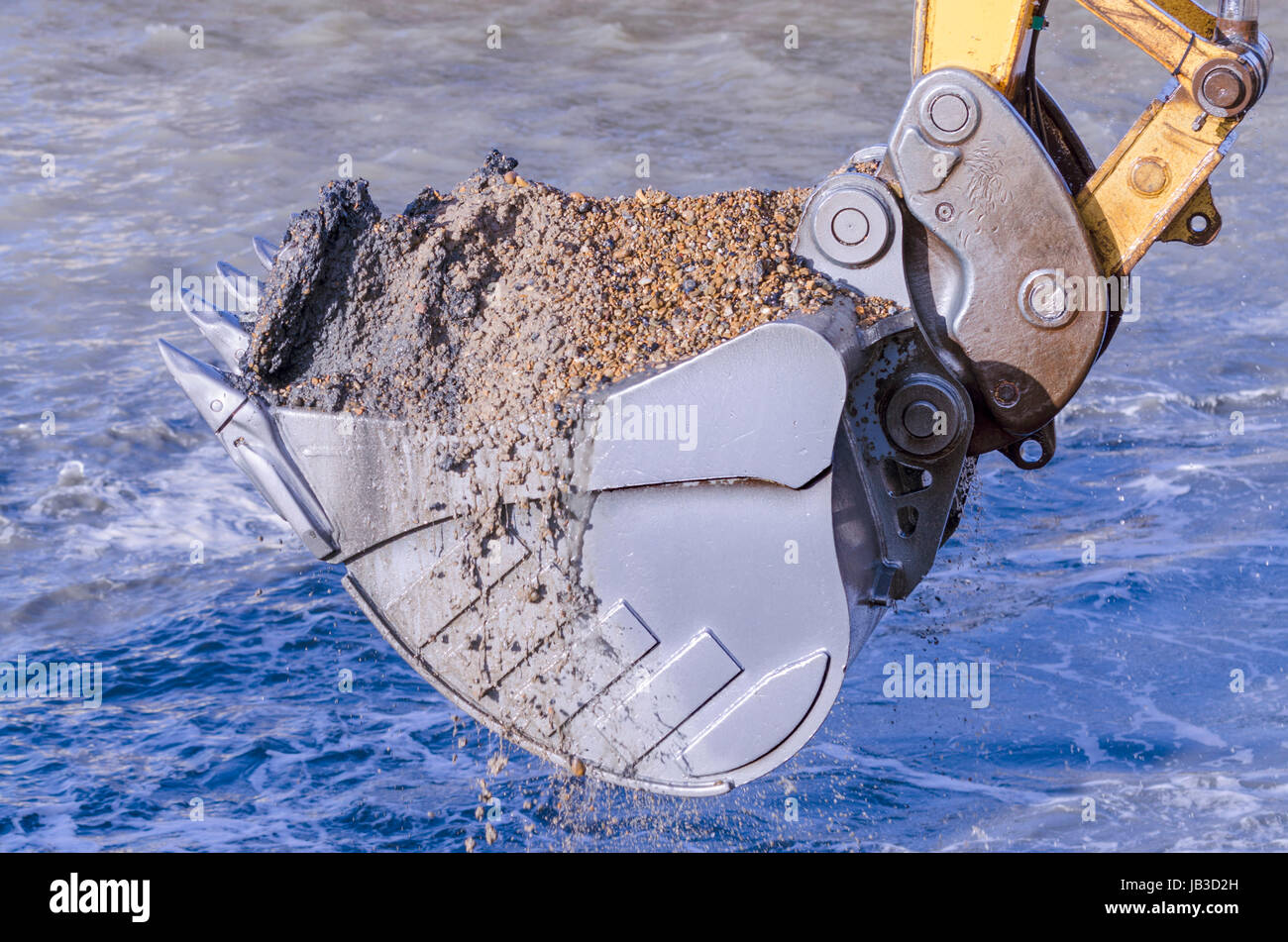Excavator bucket dredging sand and gravel from the seafront Stock Photo ...