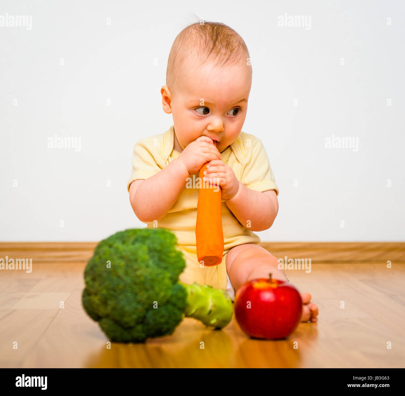Healthy living. Baby eating fruit and vegetables - sitting on floor ...