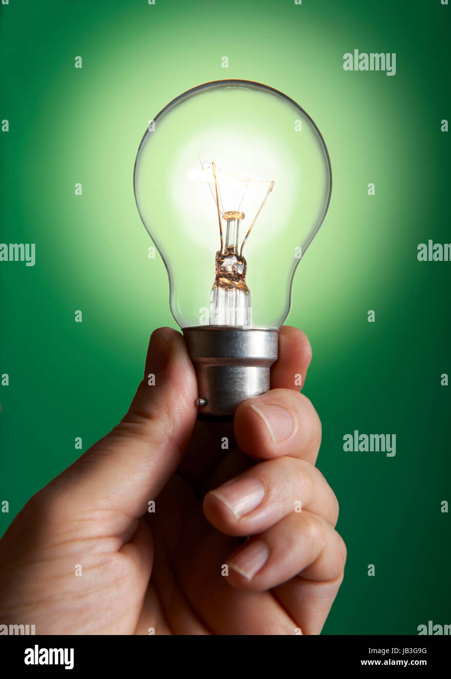 Mans hand holding a light bulb against green background Stock Photo - Alamy