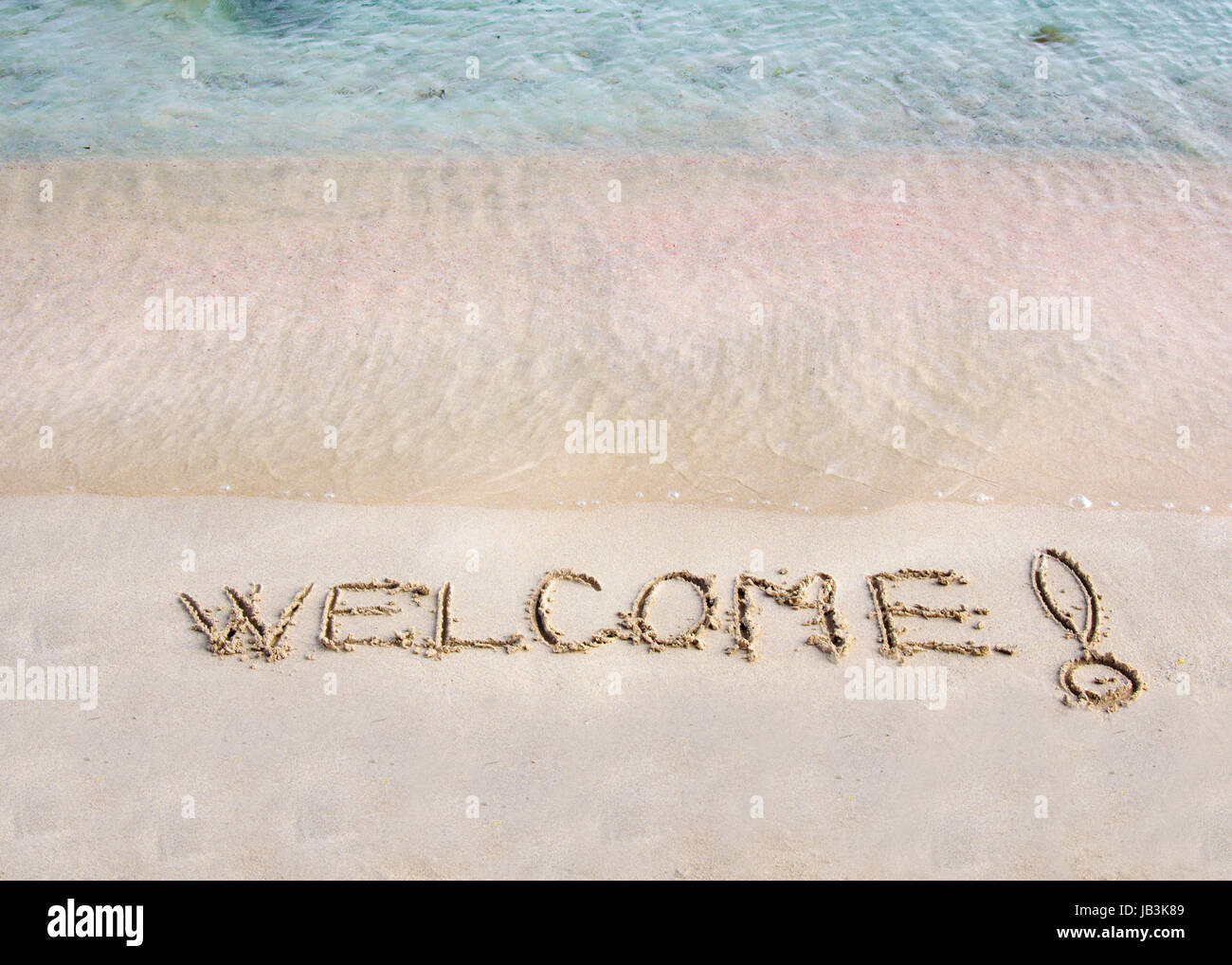 Welcome message written on white sand, with tropical sea waves in ...
