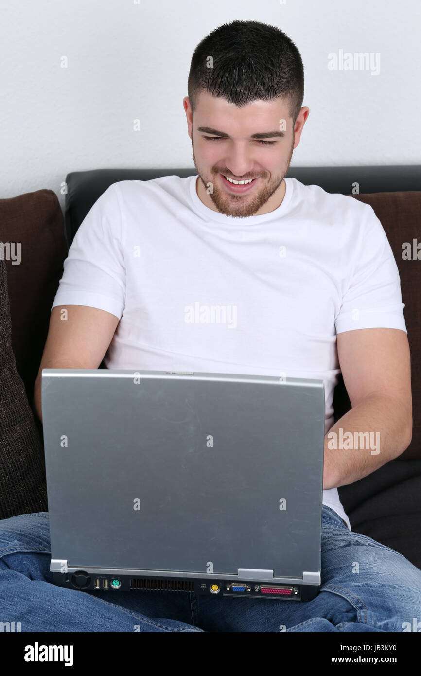 Ein junger Mann sitzt mit seinem Laptop Computer auf dem Sofa Stock ...