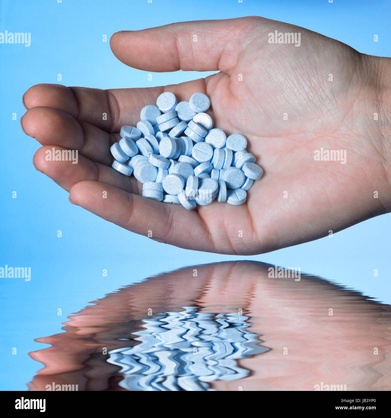 right hand holding lots of blue pills over reflective water surface in blue back Stock Photo - Alamy
