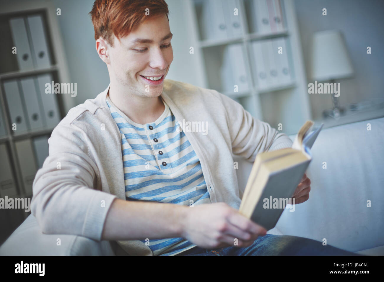 Portrait of young guy in casual clothes reading book at home Stock ...