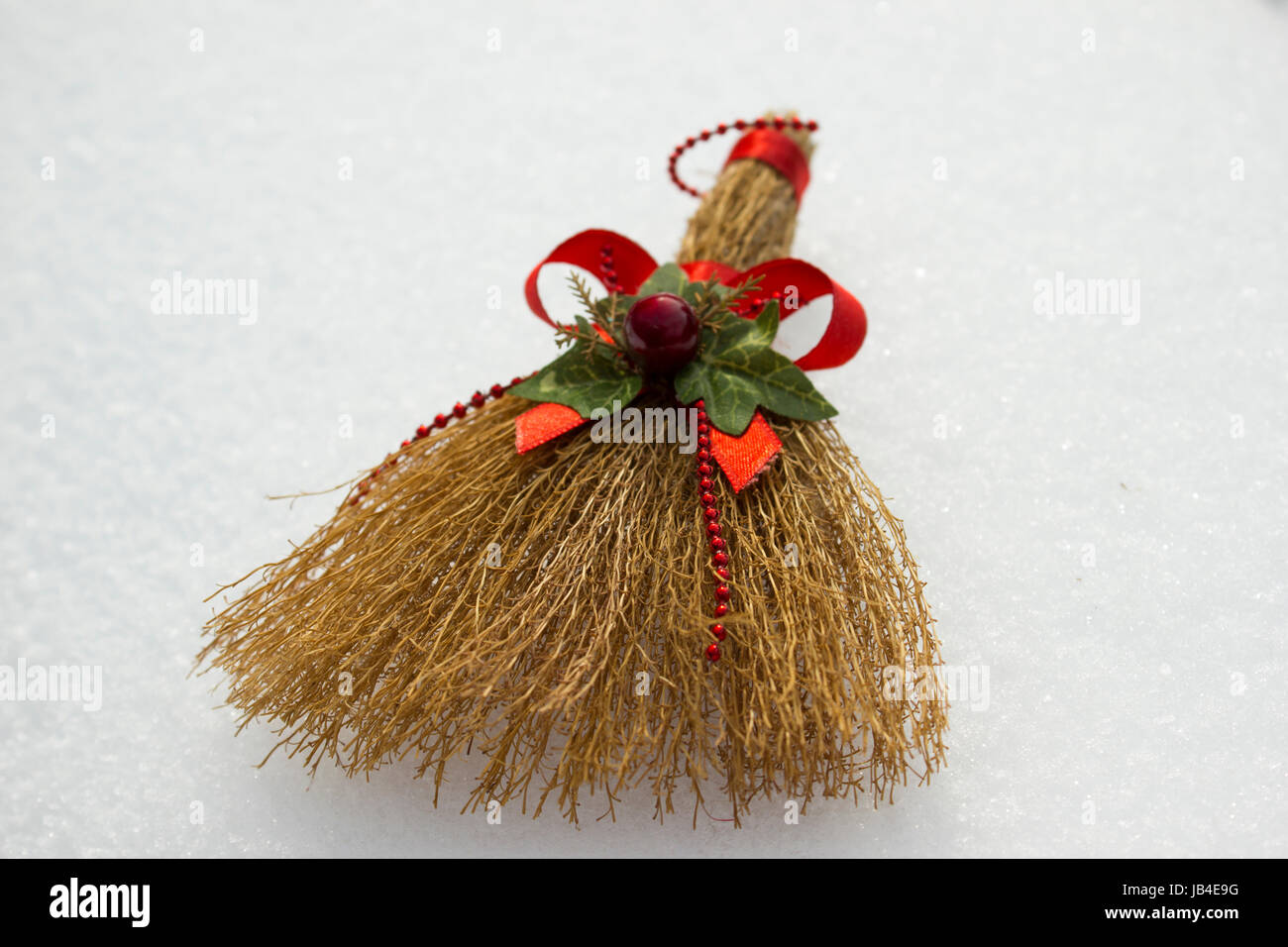 Toy broom with red ribbon and holiday ornaments laying around the snow ...