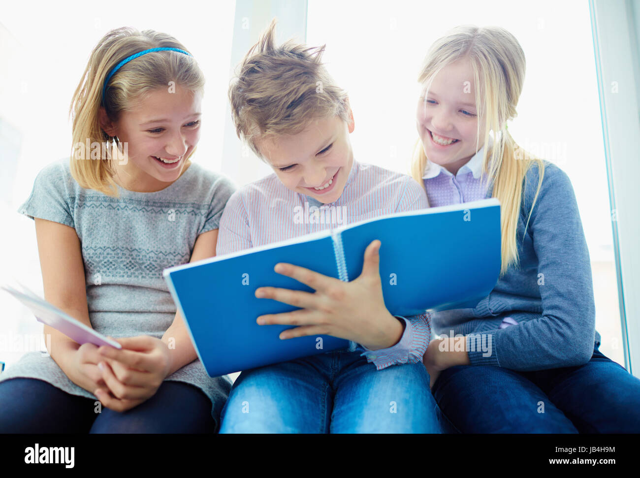Portrait of three laughing classmates looking at notes in exercise book ...