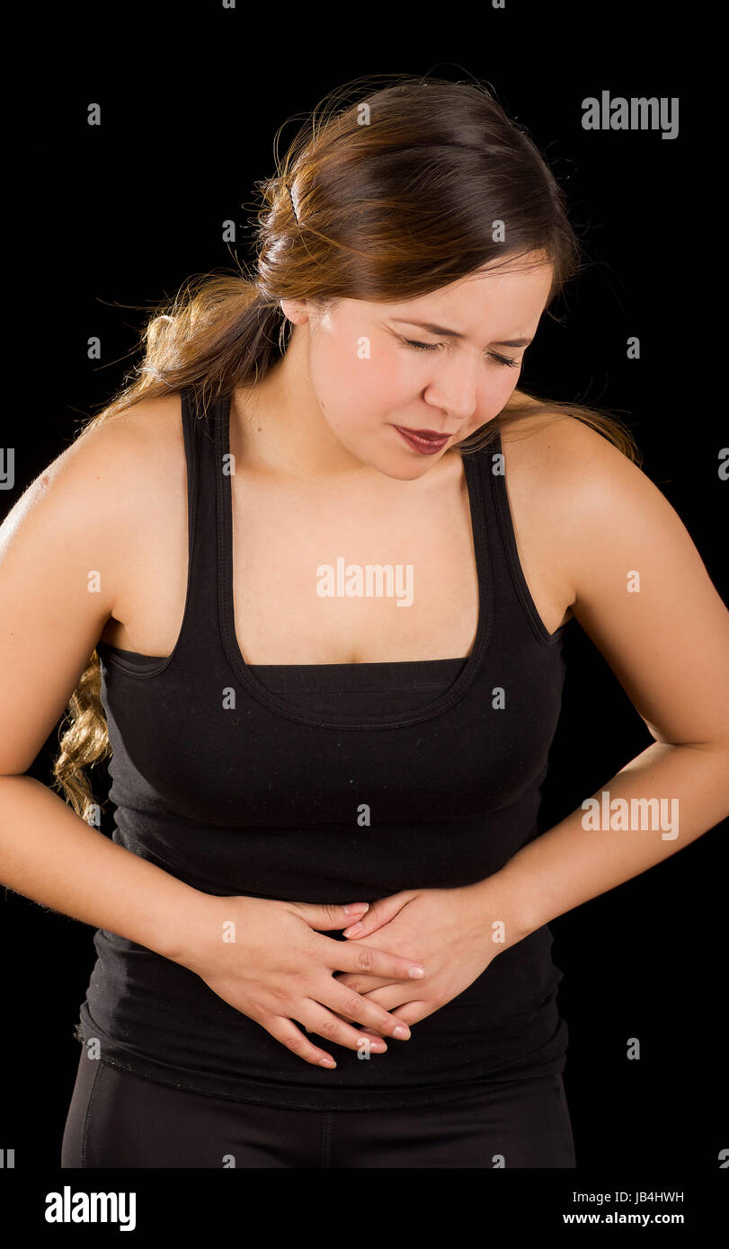Beautiful young woman with stomach ache or nausea in a black background ...