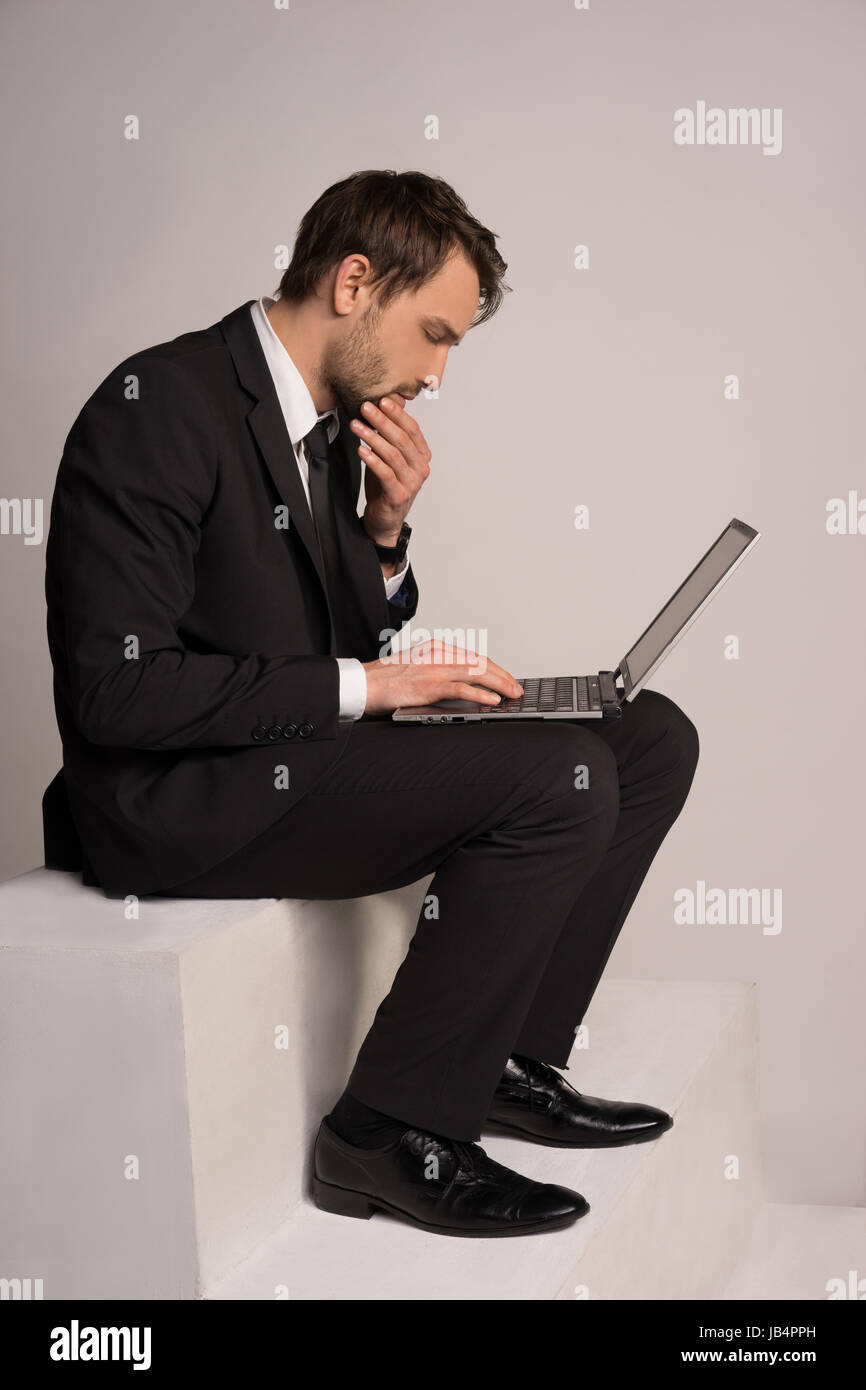 Businessman sitting on a stair working on a laptop computer balanced on ...