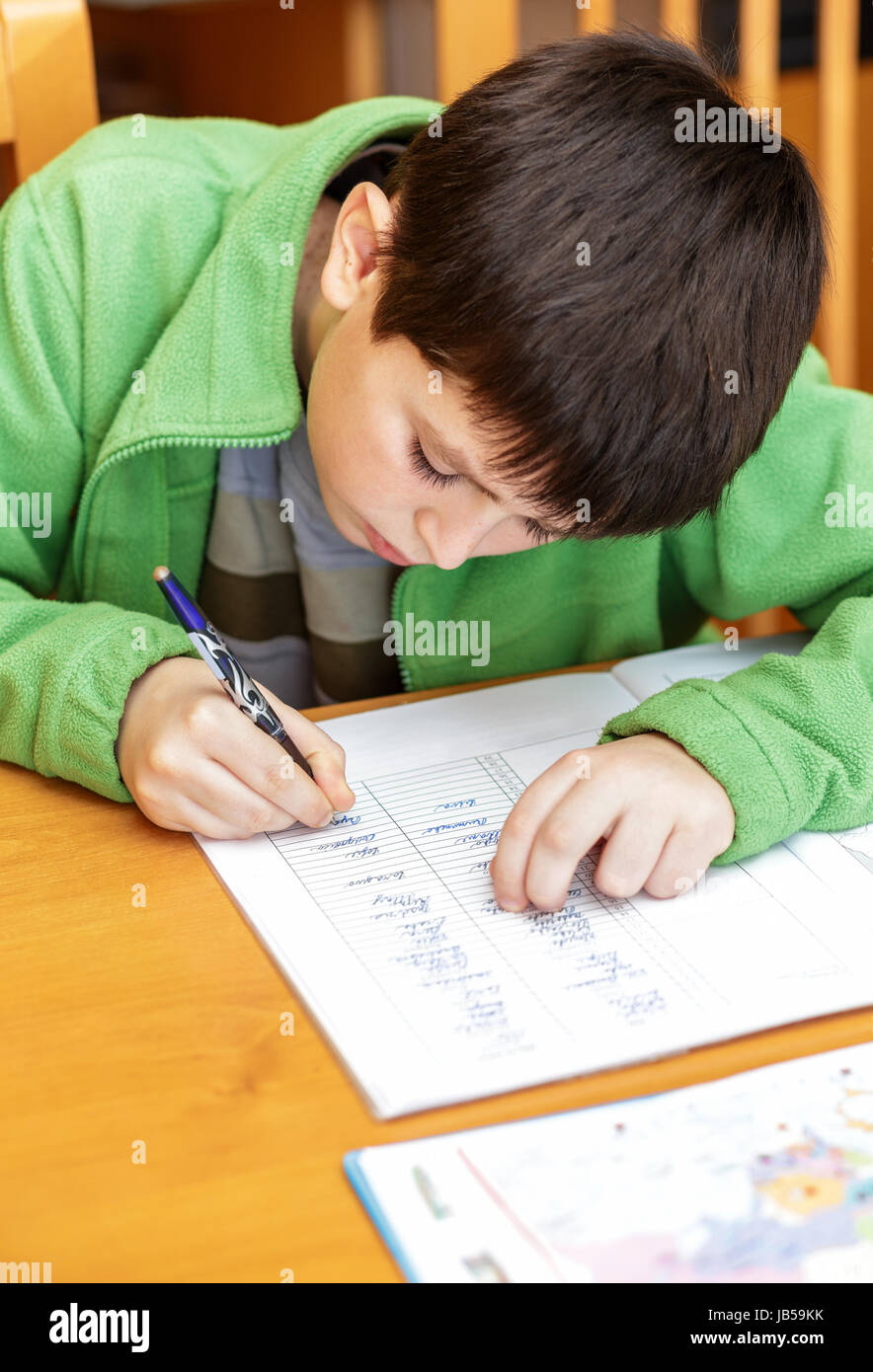 bored and tiredboy doing homework from school in workbook using worl ...