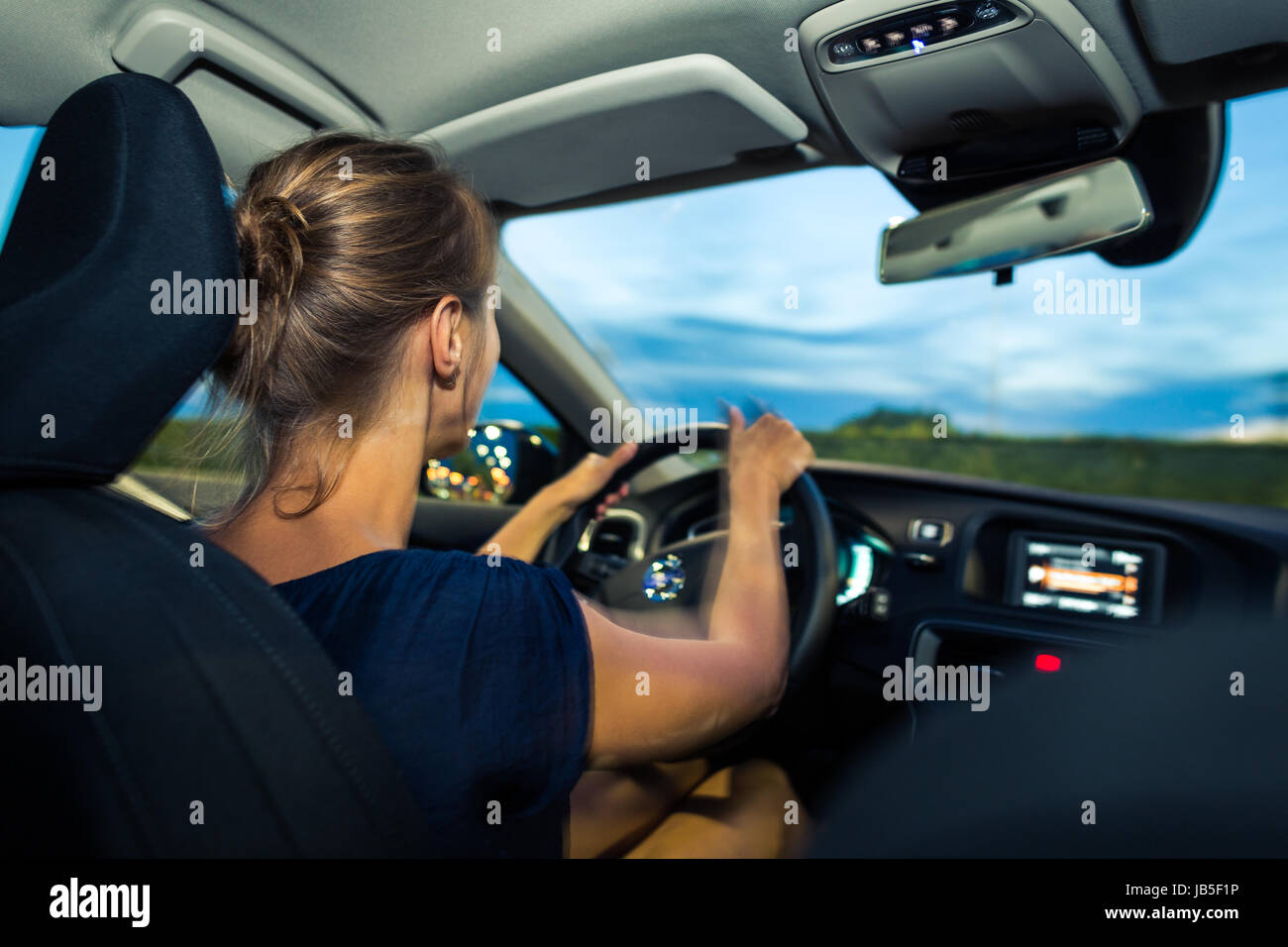 Young, woman driving a car at dusk, going home from work (long exposure ...