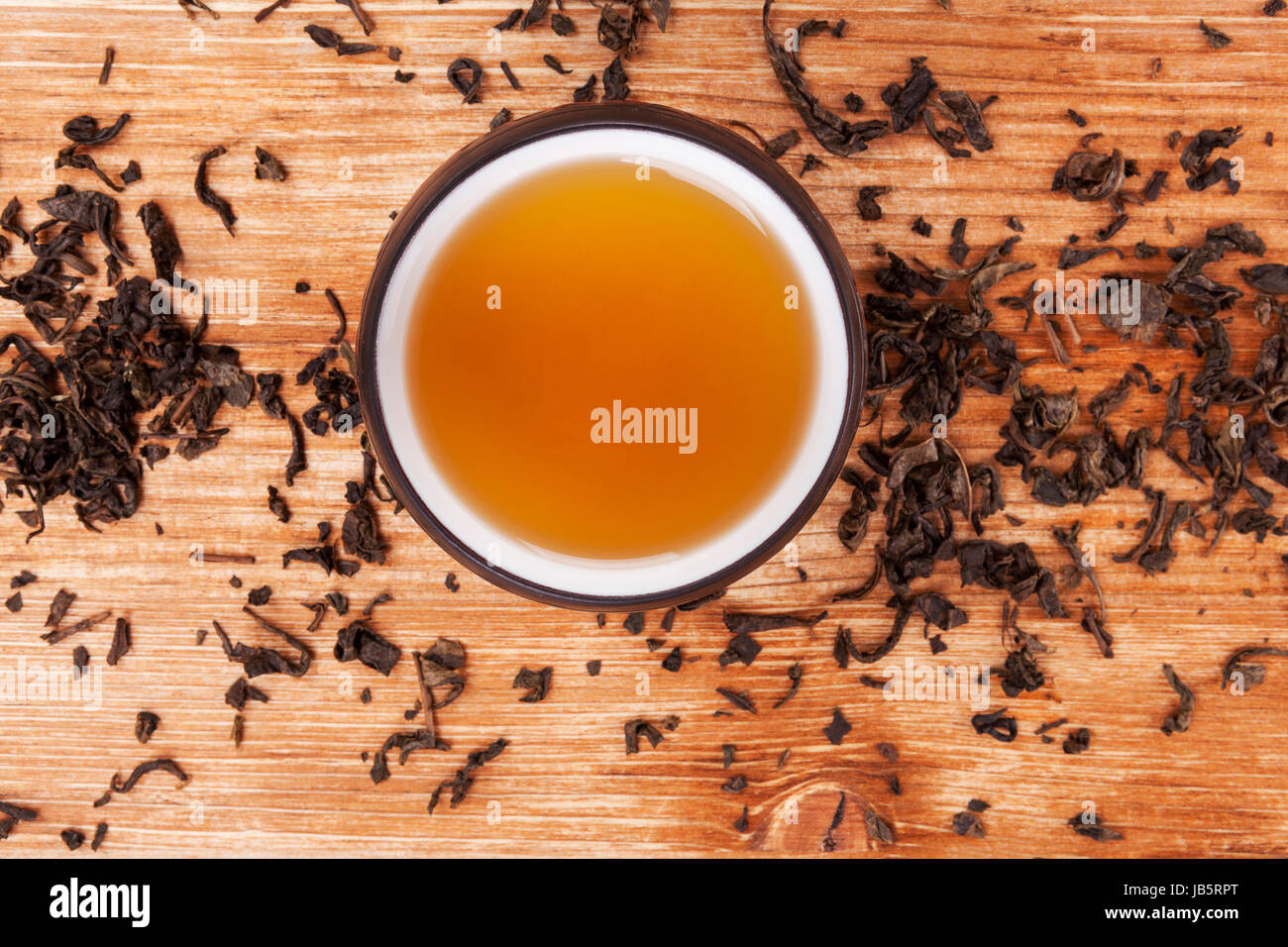 Mug of hot delicious green tea surrounded with dried leaves on wooden ...