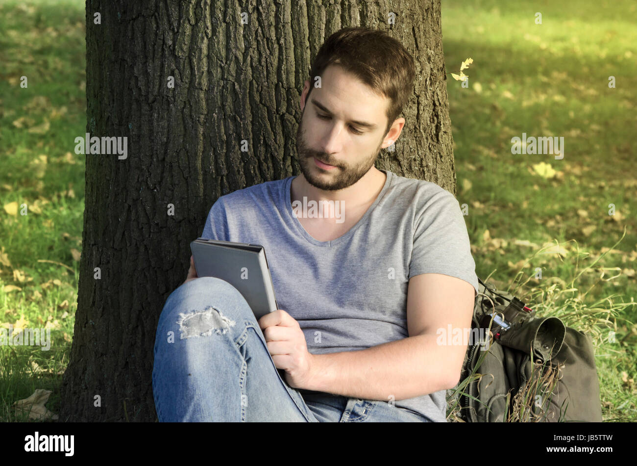 Young man reading e-book under the tree Stock Photo - Alamy