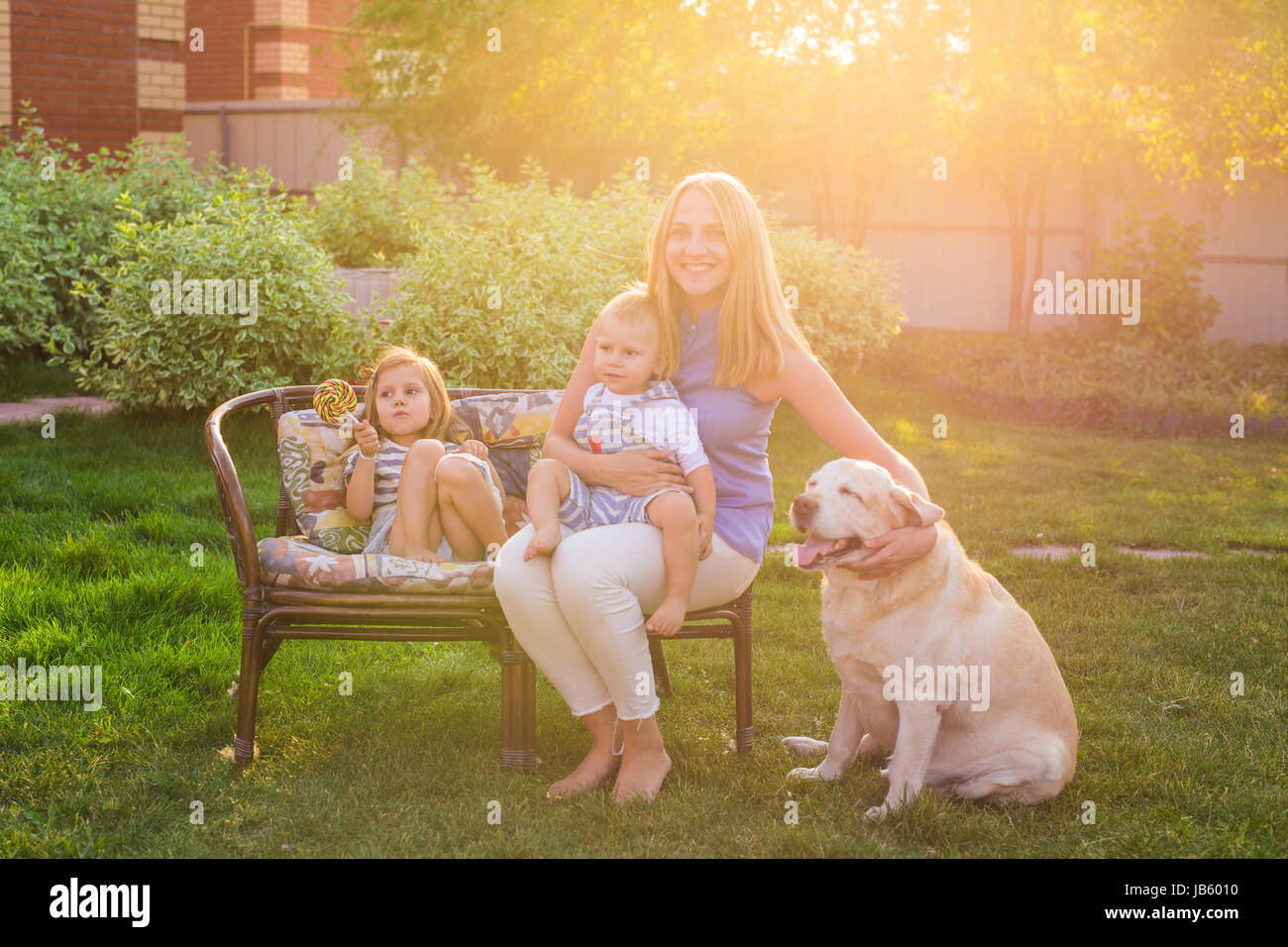 Happy mother and two children with Golden Retriever dog in the garden ...