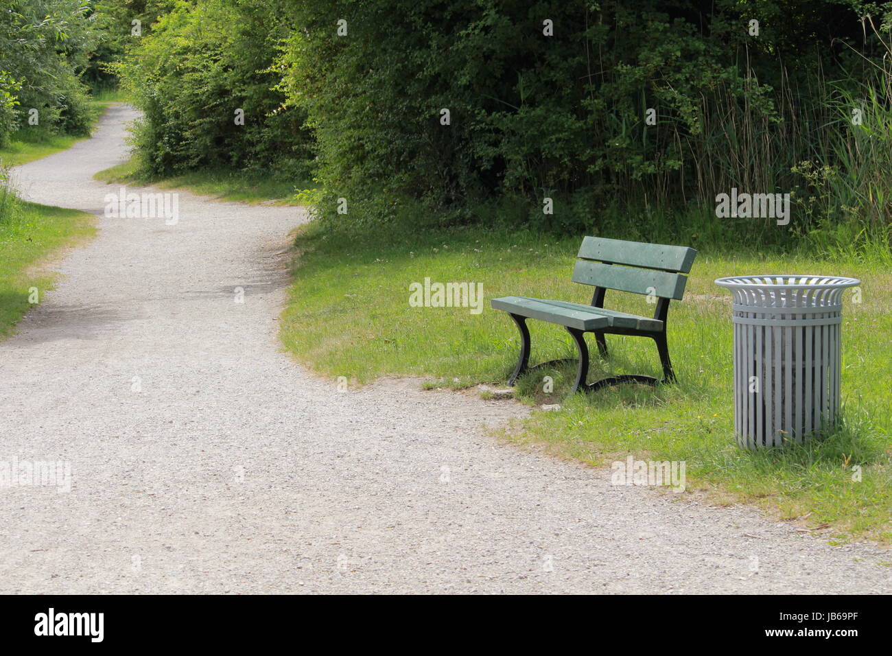 A bench and trash can placed in the grass facing a path Stock Photo - Alamy