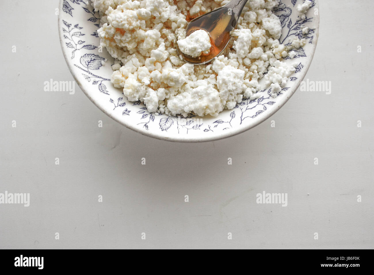 Curd crumbly in a plate on a white background with honey and a spoon ...