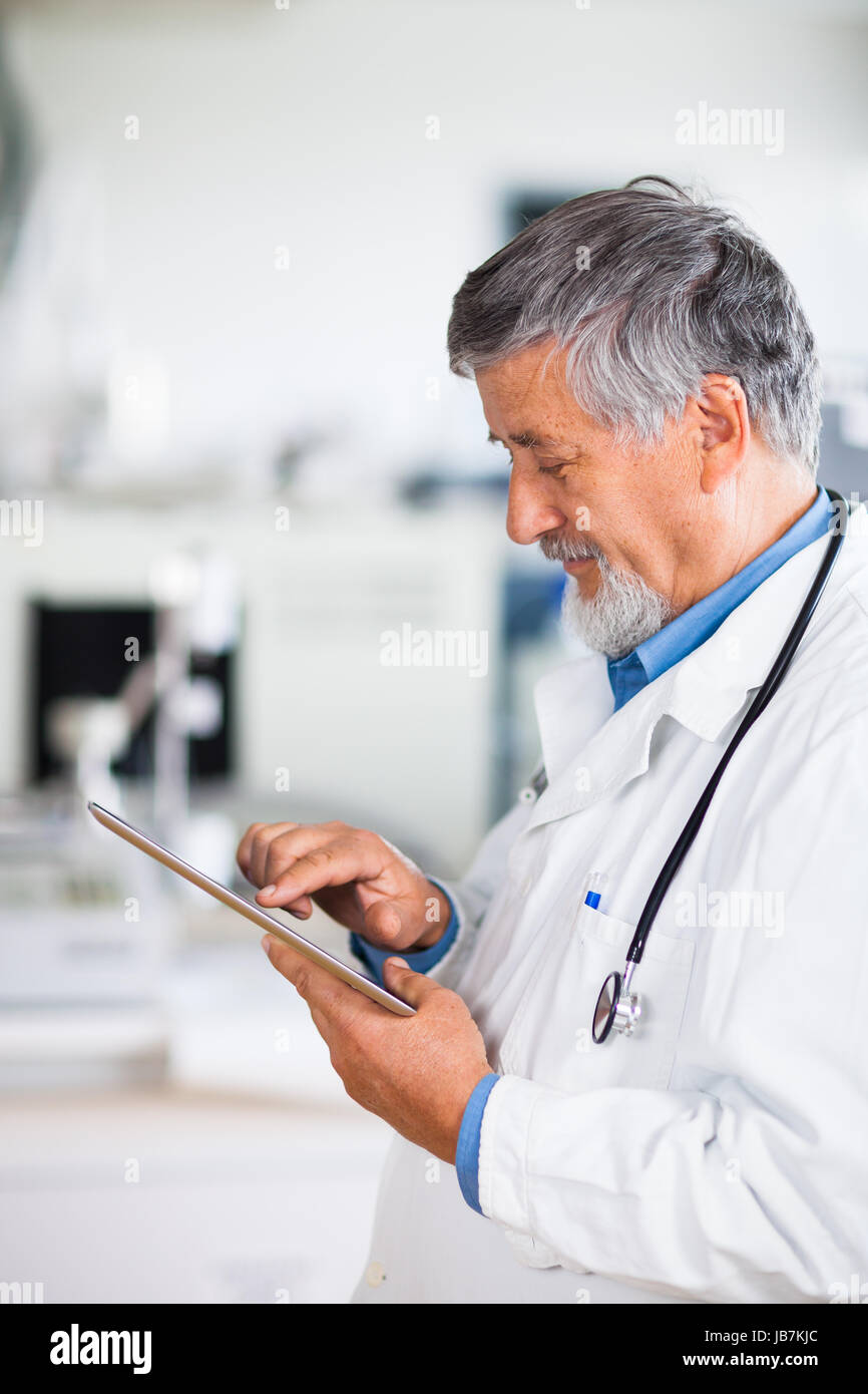 Senior doctor using his tablet computer at work (color toned image ...