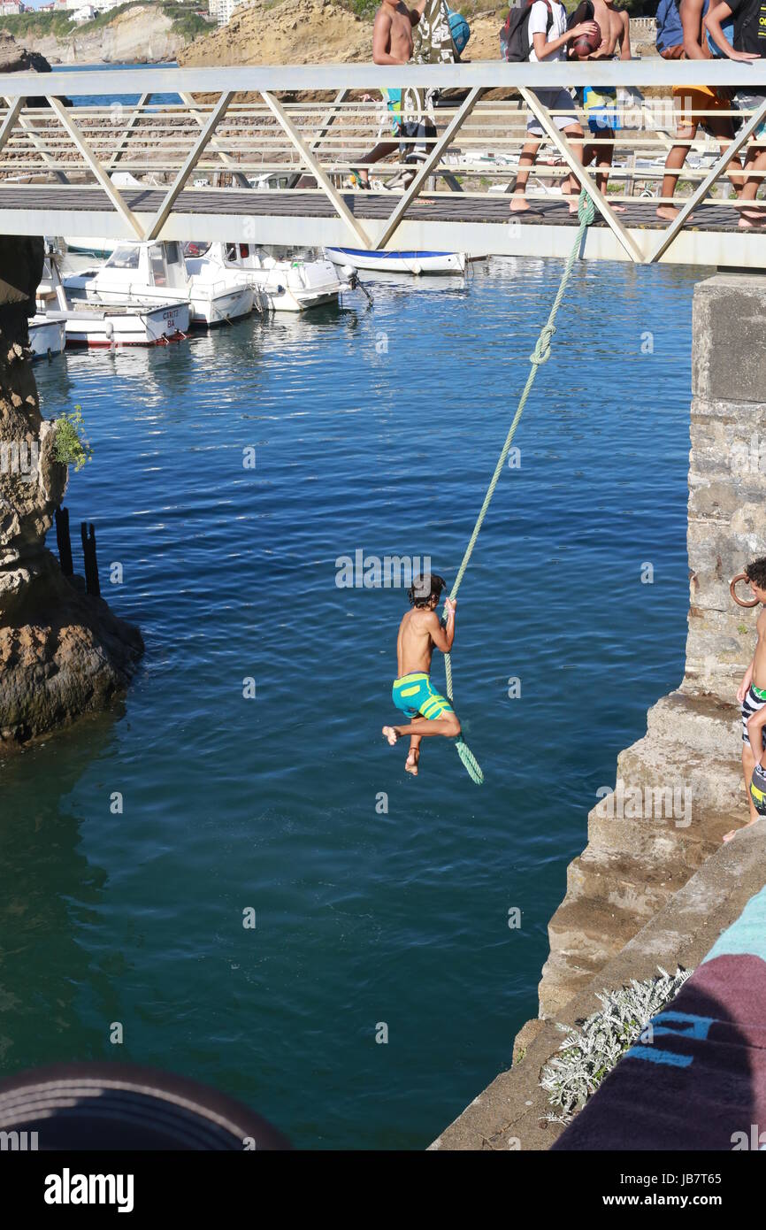 Boy swinging from bridge on rope swing in harbour area in Biarritz ...