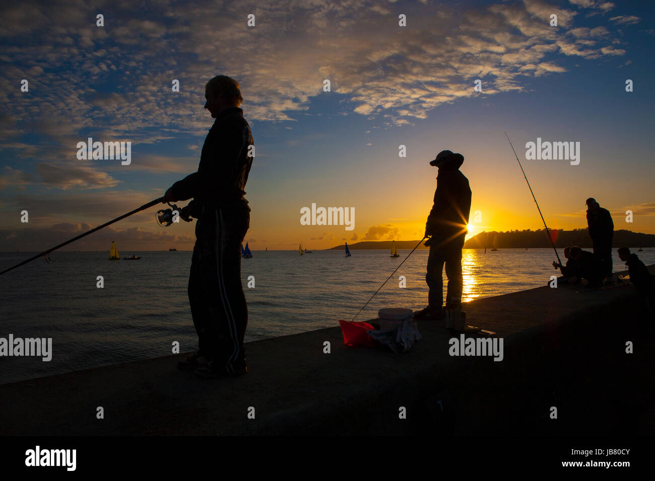 Fisherman line fishing with rods at sunset off pier into the sea ocean ...