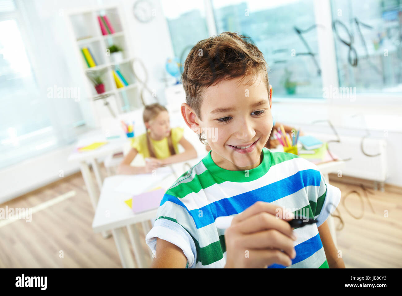 Portrait of clever boy doing sums on transparent board with schoolmate ...