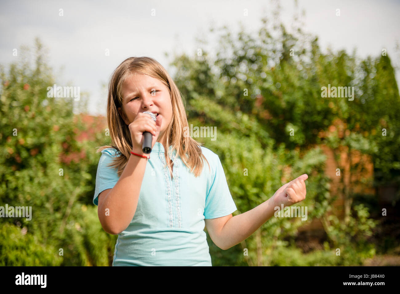 Happy childhood - child singing with microphone outdoor in backyard ...