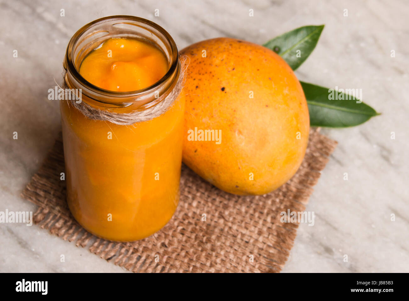 Homemade Mango Jam with fresh fruits and leaves of mango on a white ...
