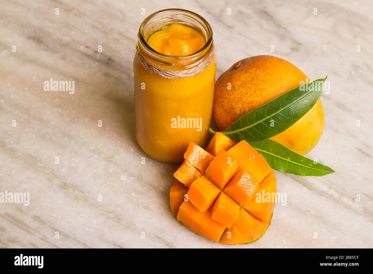 Homemade Mango Jam with fresh fruits and leaves of mango on a white ...