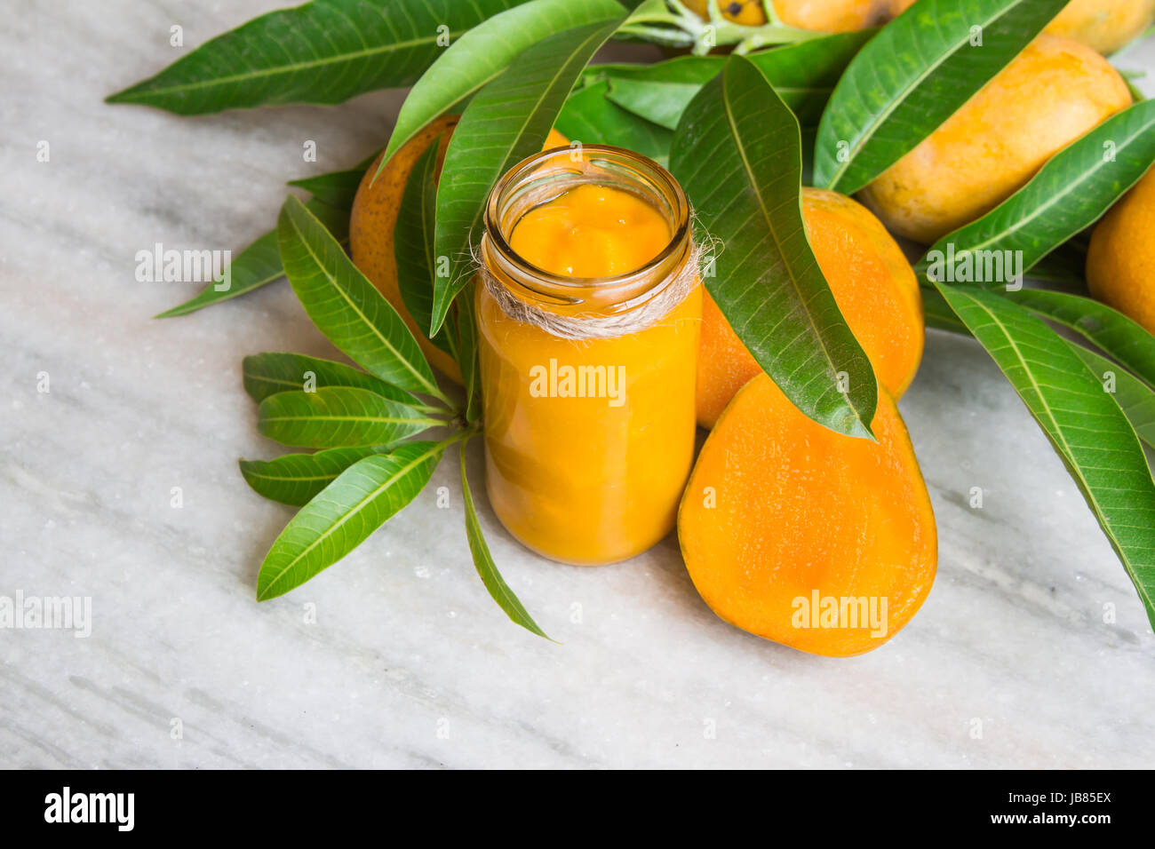 Homemade Mango Jam with fresh fruits and leaves of mango on a white ...