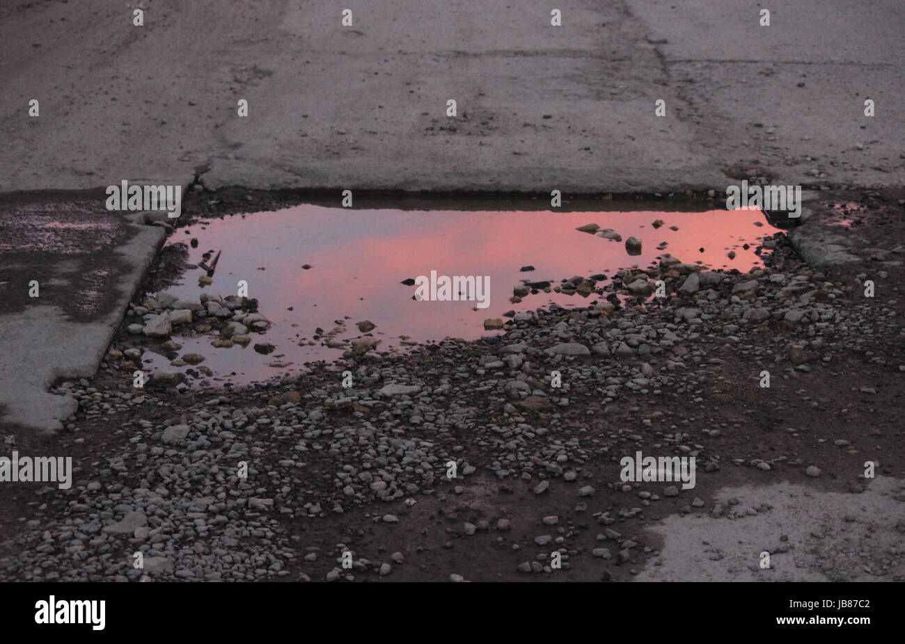 Sunset sky with clouds reflected in a puddle on a road of concrete ...