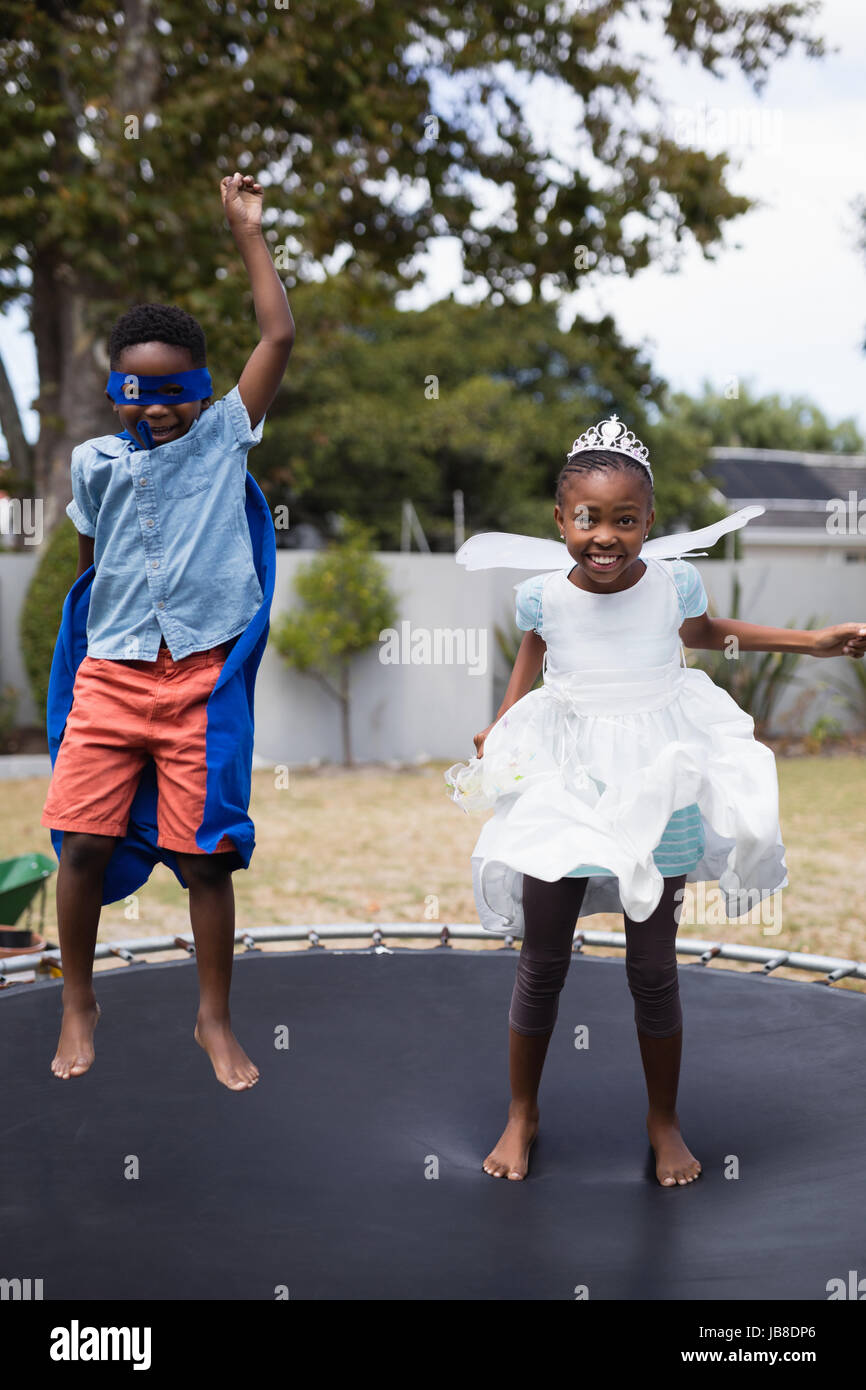 Playful siblings in costumes jumping on trampoline at lawn Stock Photo ...