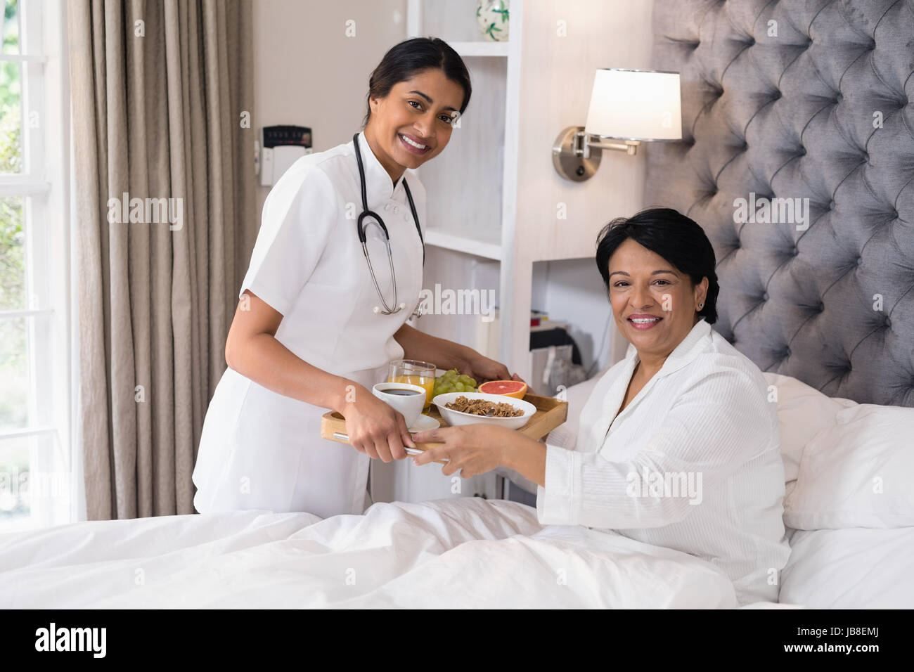 Portrait of smiling nurse serving breakfast to patient resting on bed ...