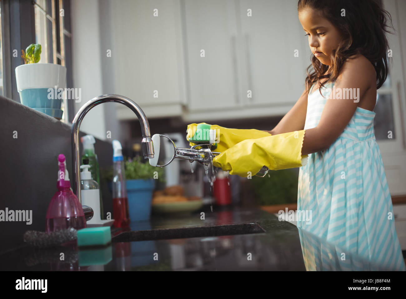 Cute little girl washing utensil in kitchen sink at home Stock Photo ...