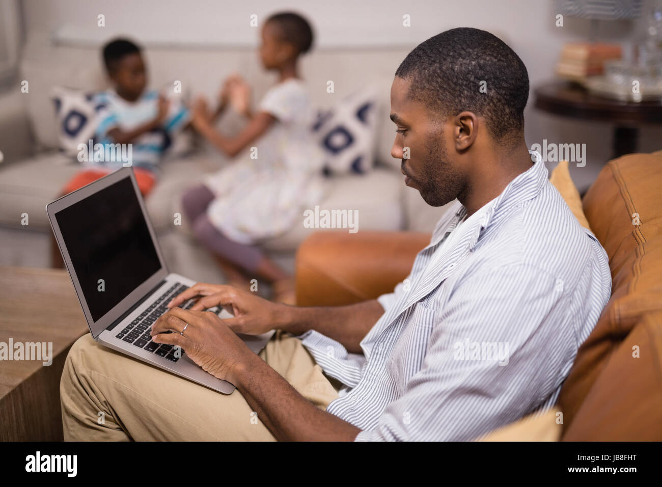 Side view of young man using laptop while children playing at home ...