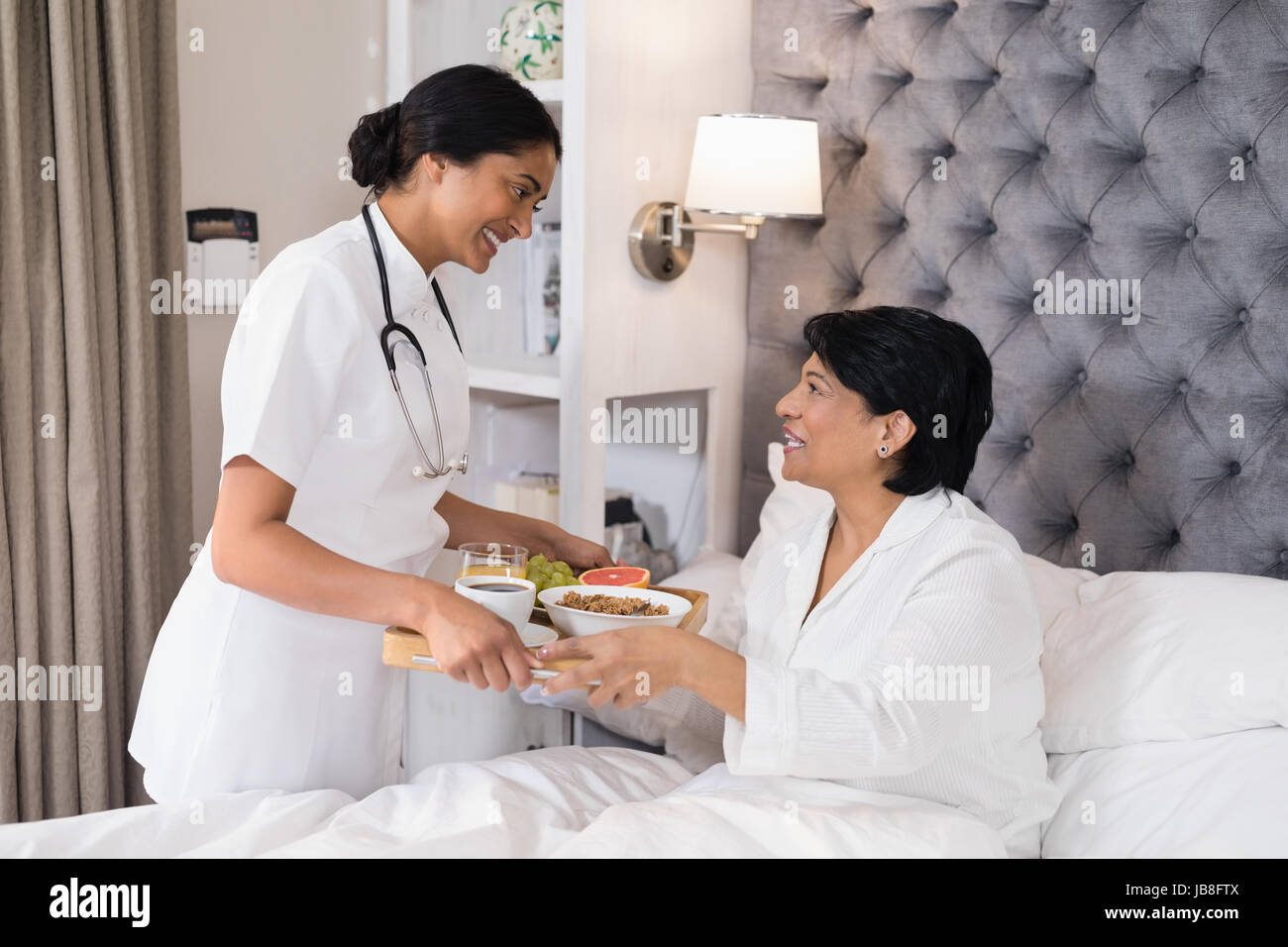 Smiling nurse serving breakfast to patient resting on bed at home Stock ...