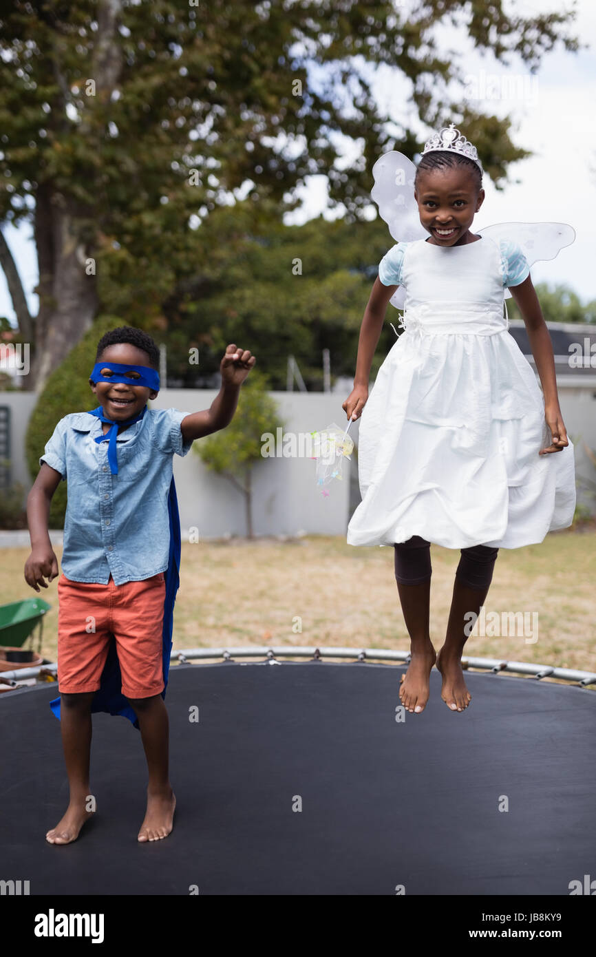 Full length of siblings in costumes jumping on trampoline at lawn Stock ...