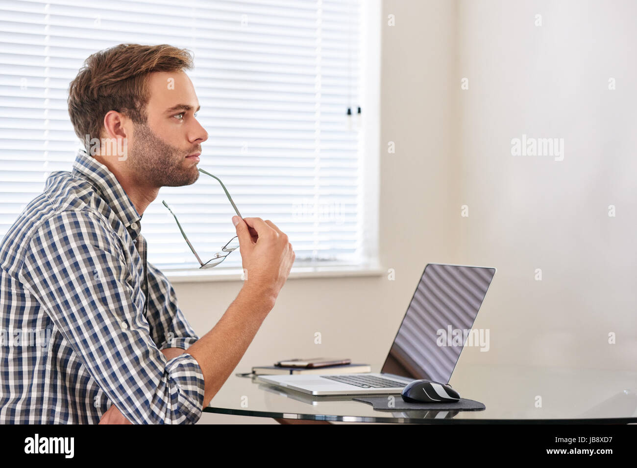 Handsome young man seated behind his laptop computer, looking into the ...