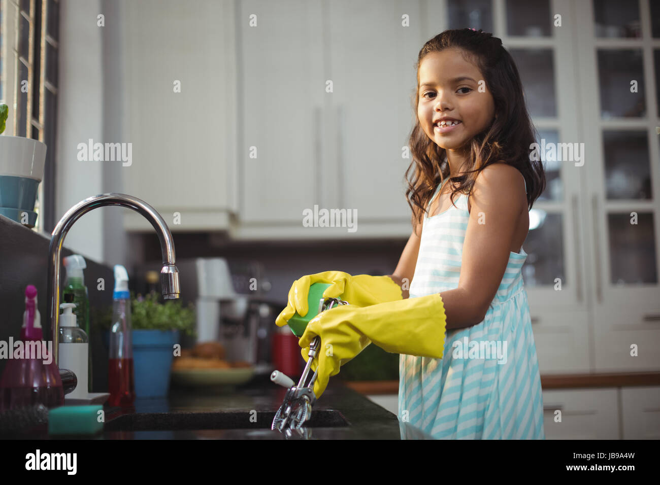 Portrait of cute little girl washing utensil in kitchen sink at home ...