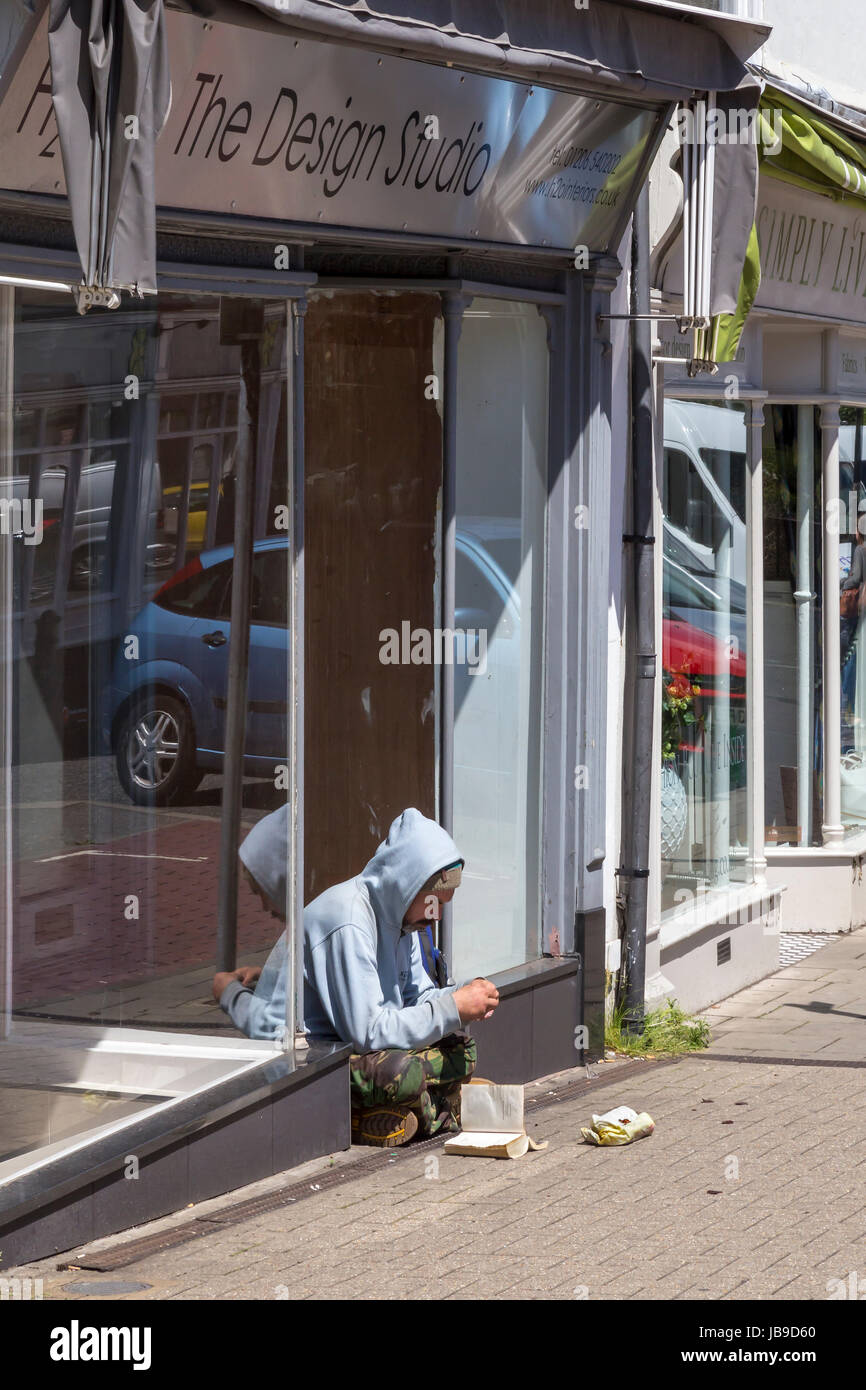 A YOUNG MAN SITS IN A CLOSED DOWN SHOP DOORWAY BEGGING FOR MONEY Stock ...