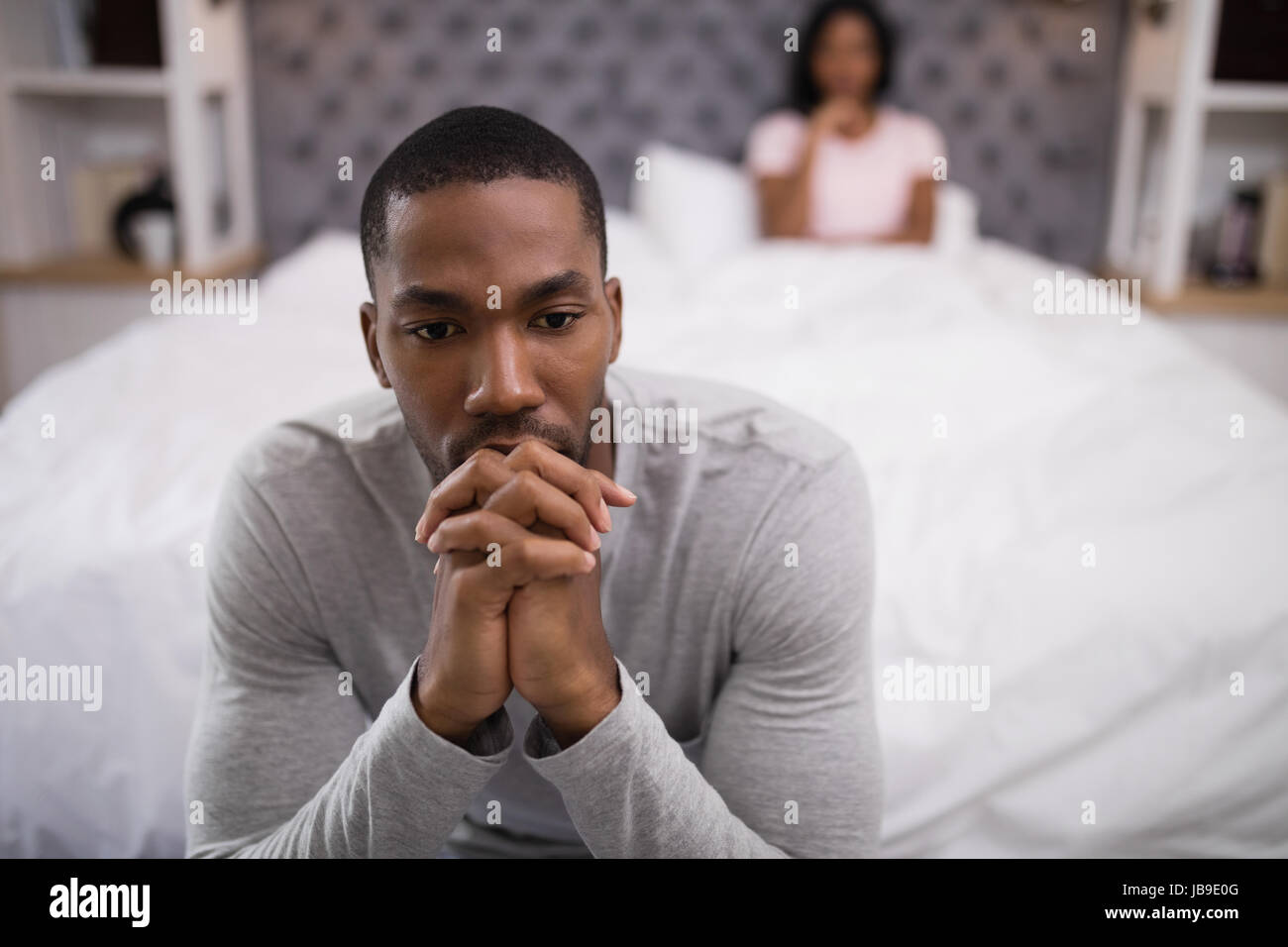 Tensed man sitting while woman lying on bed at home Stock Photo - Alamy