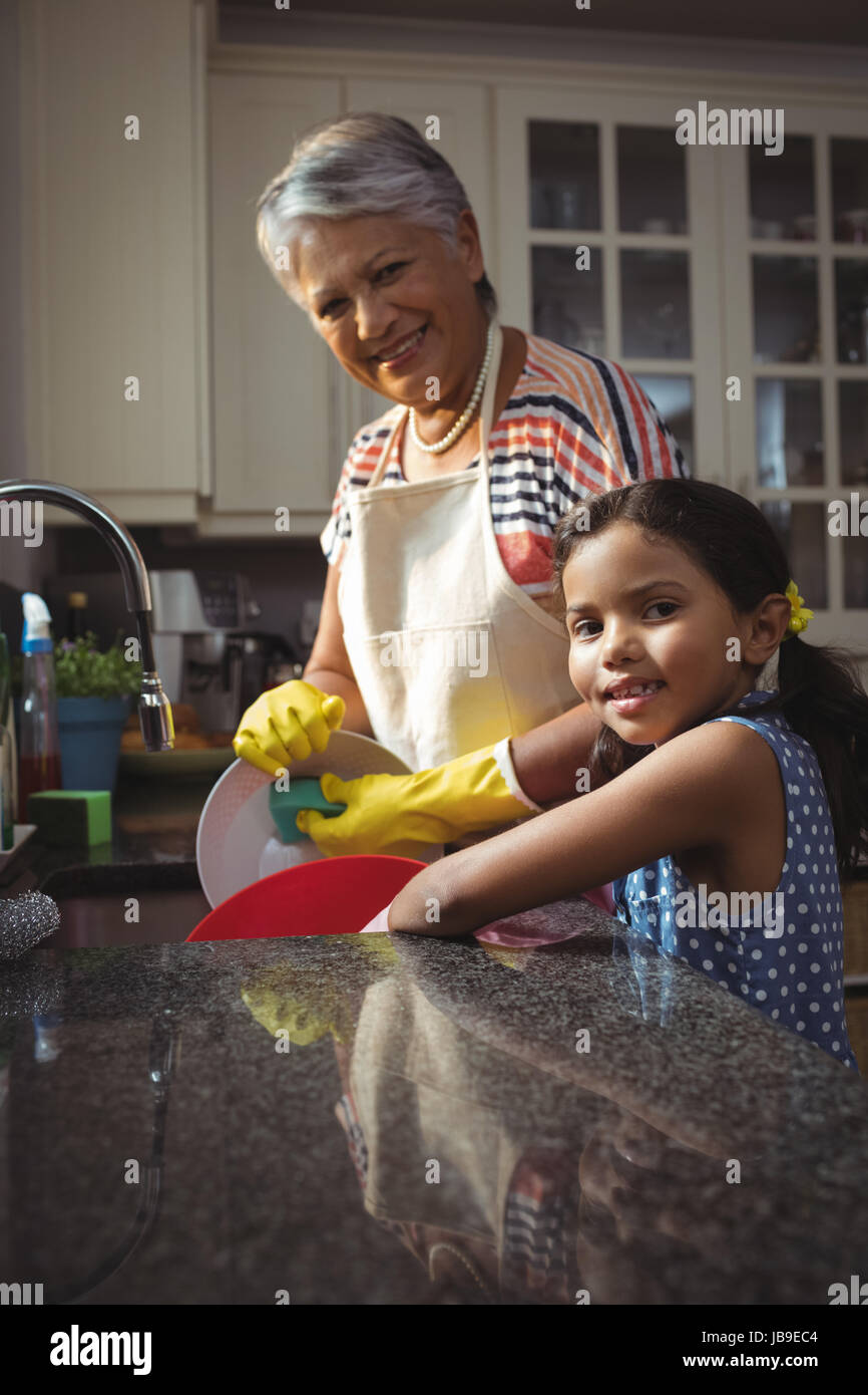 Portrait of grandmother and granddaughter washing utensil in kitchen ...