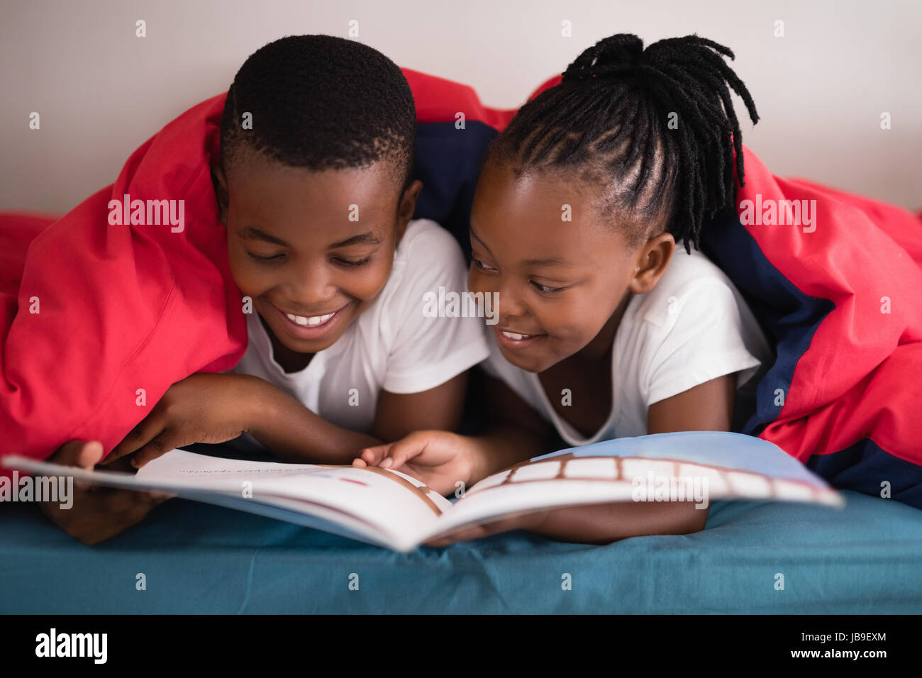 Smiling siblings reading book together while lying on bed at home Stock ...