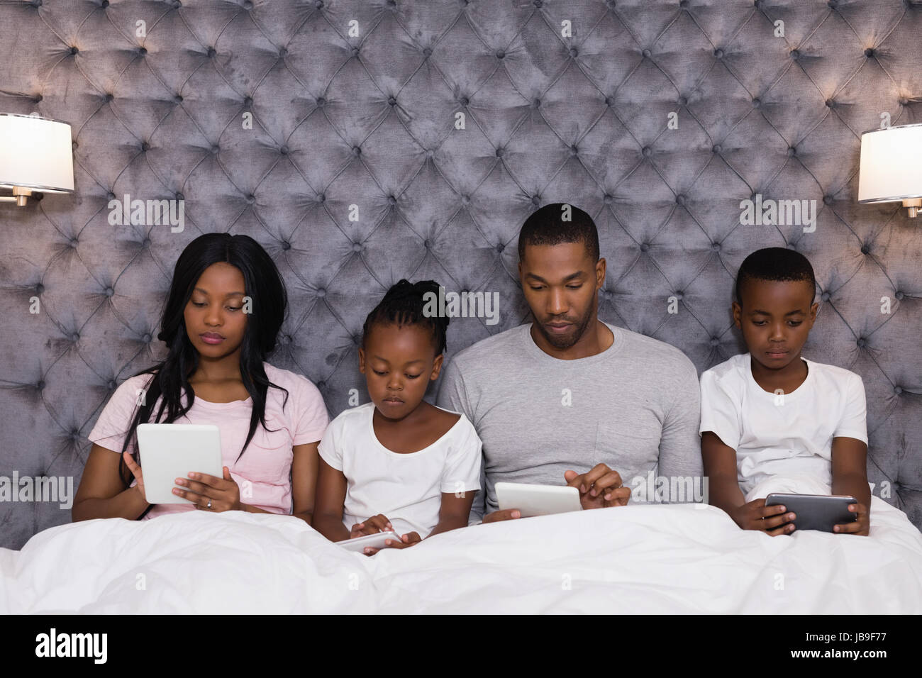 Family using digital tablets while sitting together on bed at home ...