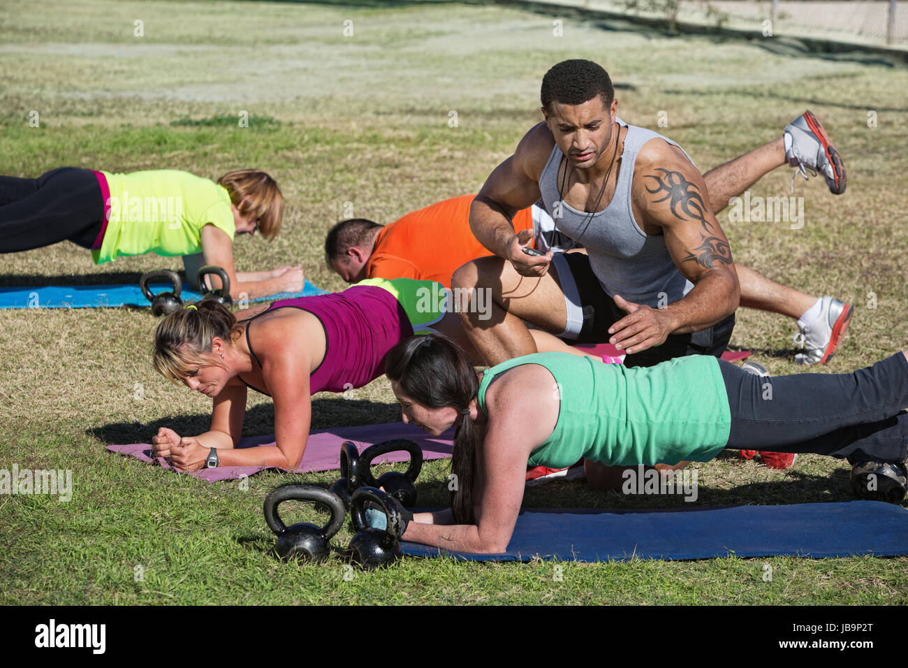 Muscular instructor with stopwatch helping students in fitness class ...