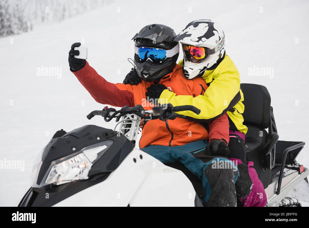Couple taking selfie on mobile phone while riding snowmobile during ...