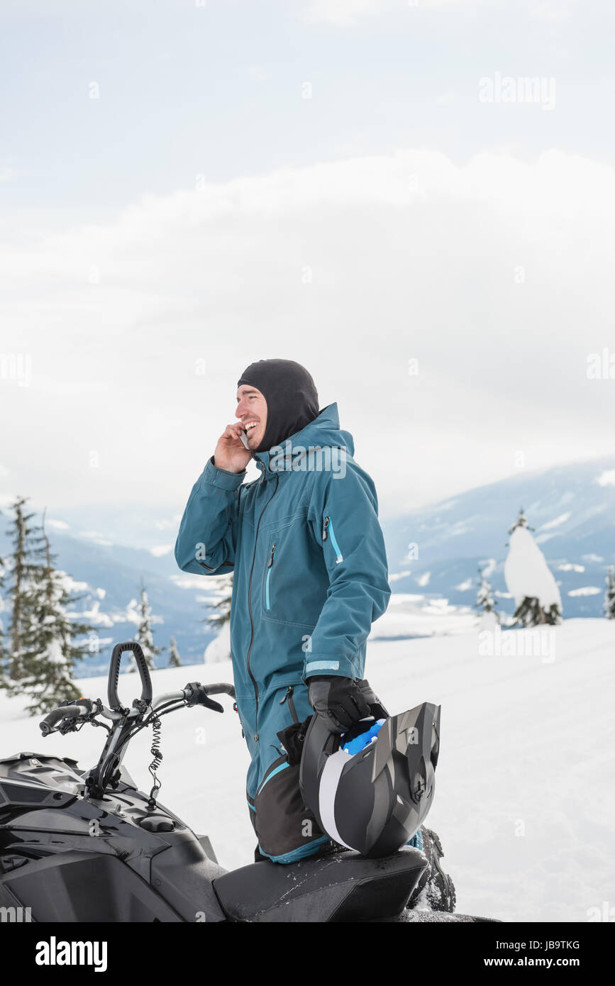 Man talking on mobile phone while standing near snowmobile in snowy ...
