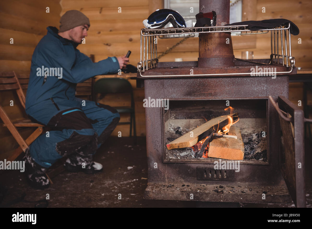 Man using mobile phone near wood burning stove at log cabin Stock Photo ...