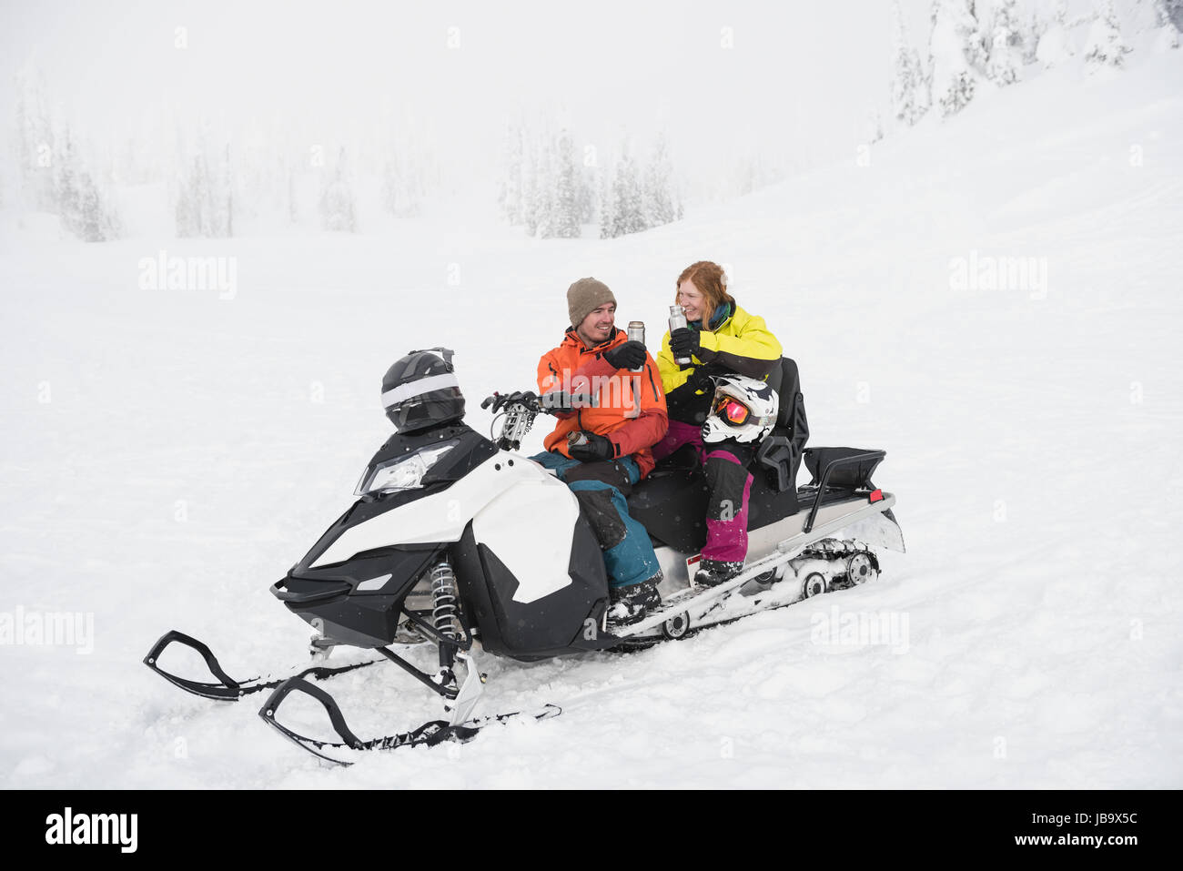 Couple having coffee from thermos while relaxing on snowmobile during ...