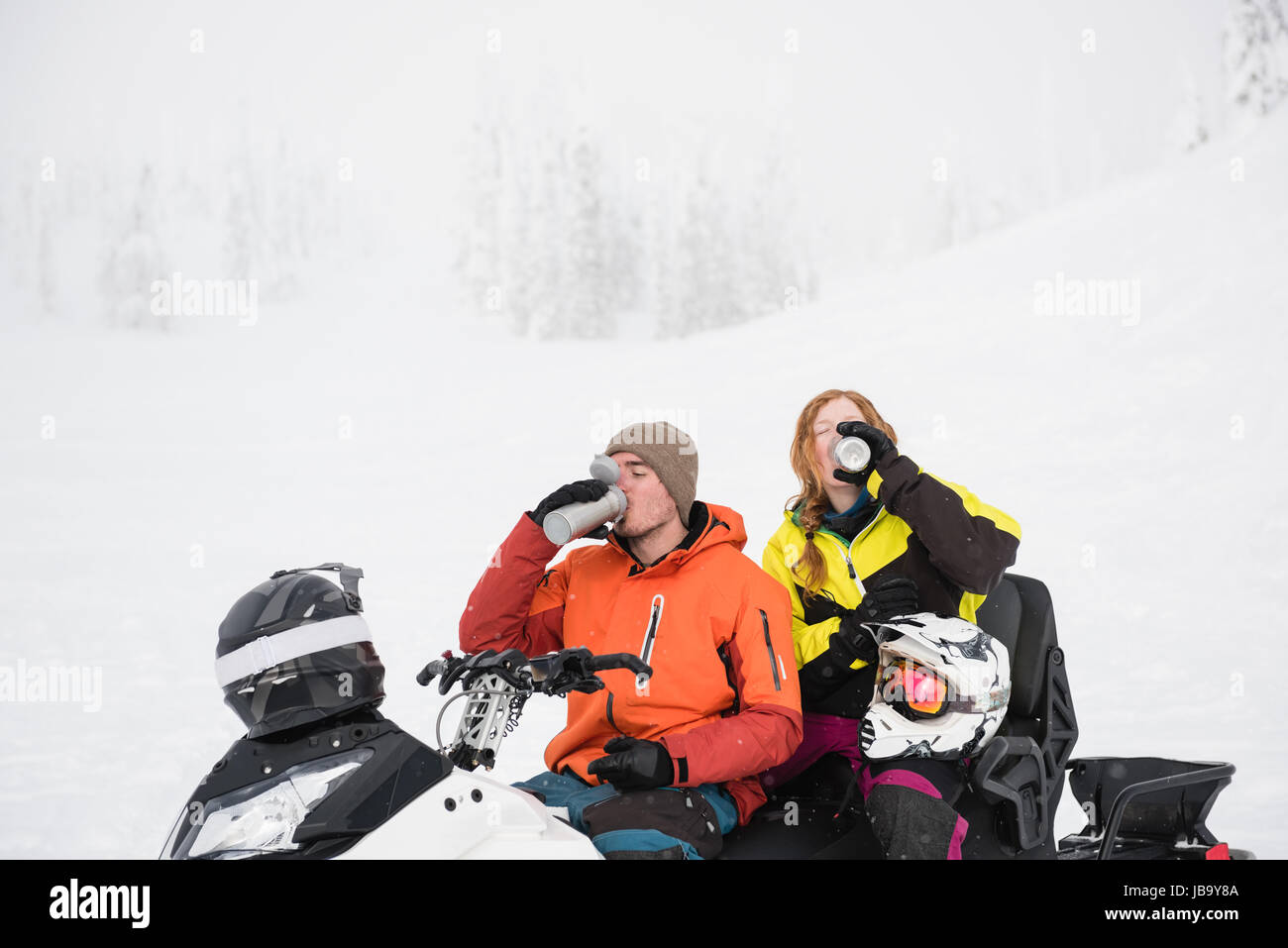 Couple having coffee from thermos while relaxing in snowmobile during ...